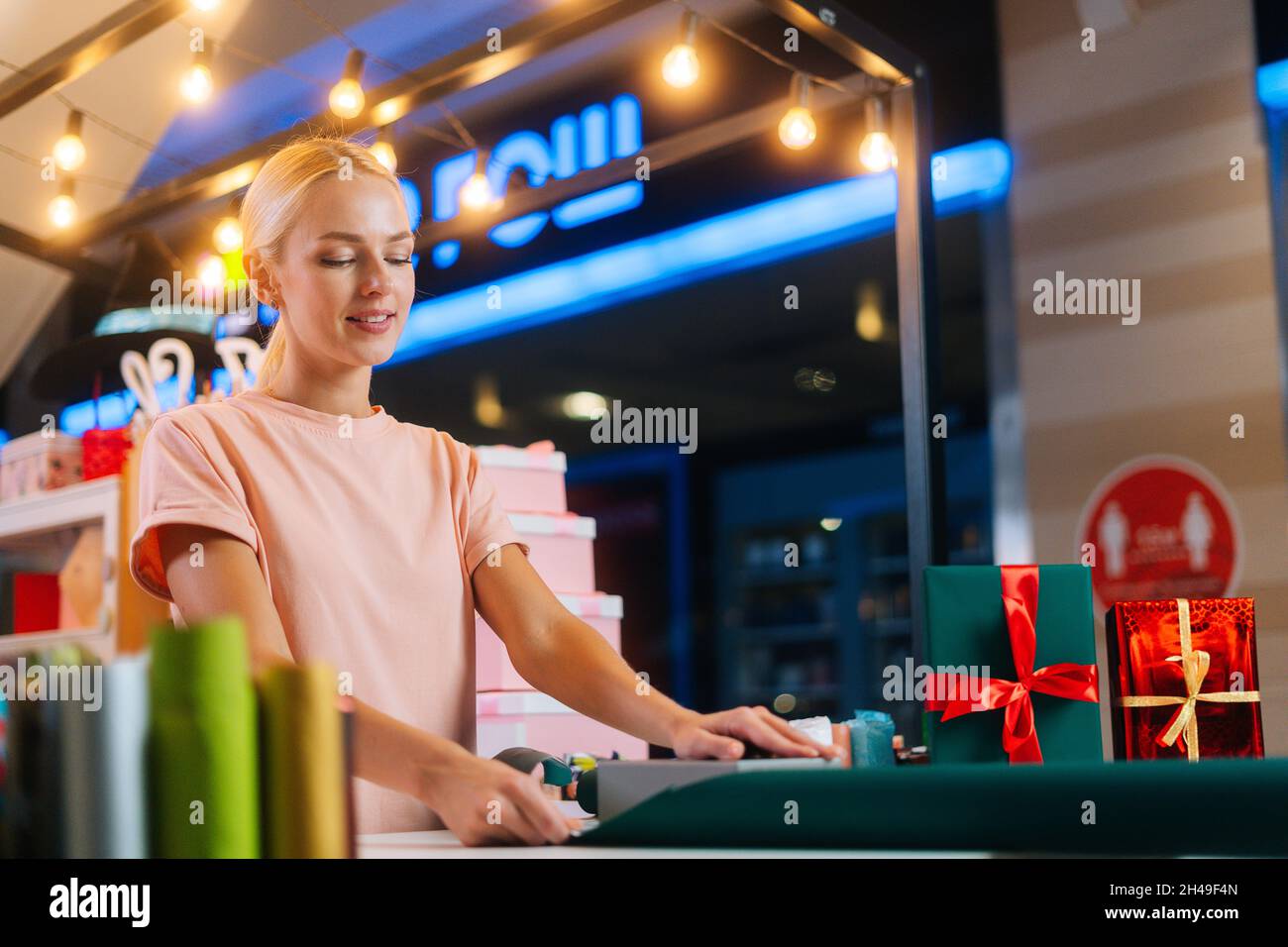 Cheerful attractive young woman wrapping festive Christmas gift box in ...