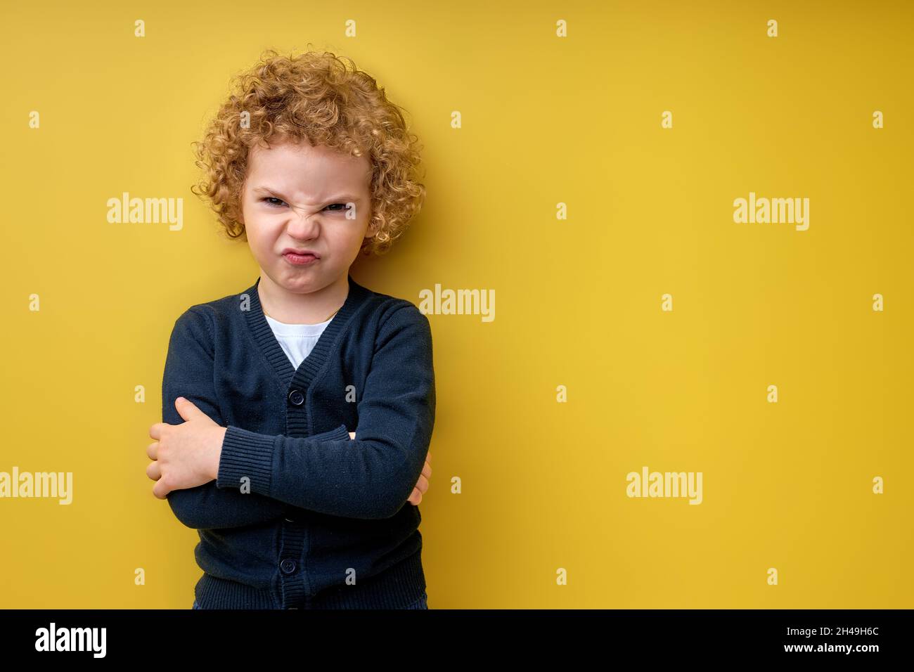 Curly offended child boy with arms folded posing at camera, isolated on ...