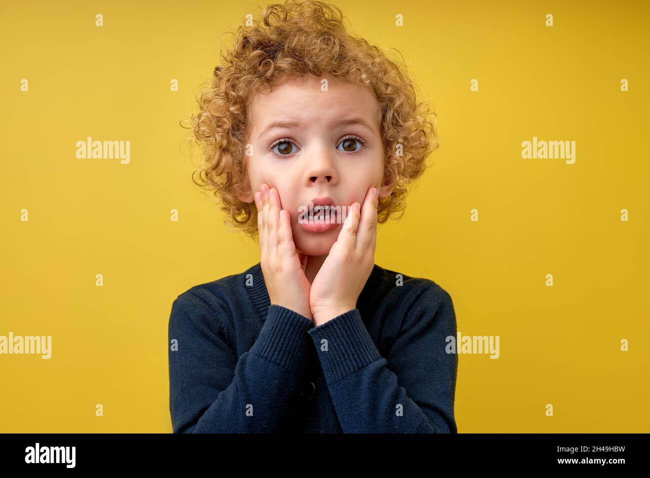 Portrait of surprised kid boy in shock, touching cheeks, stand with ...