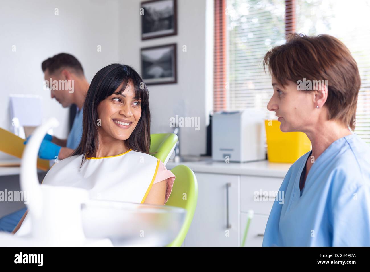 Caucasian female dental nurse talking to smiling female patient at ...