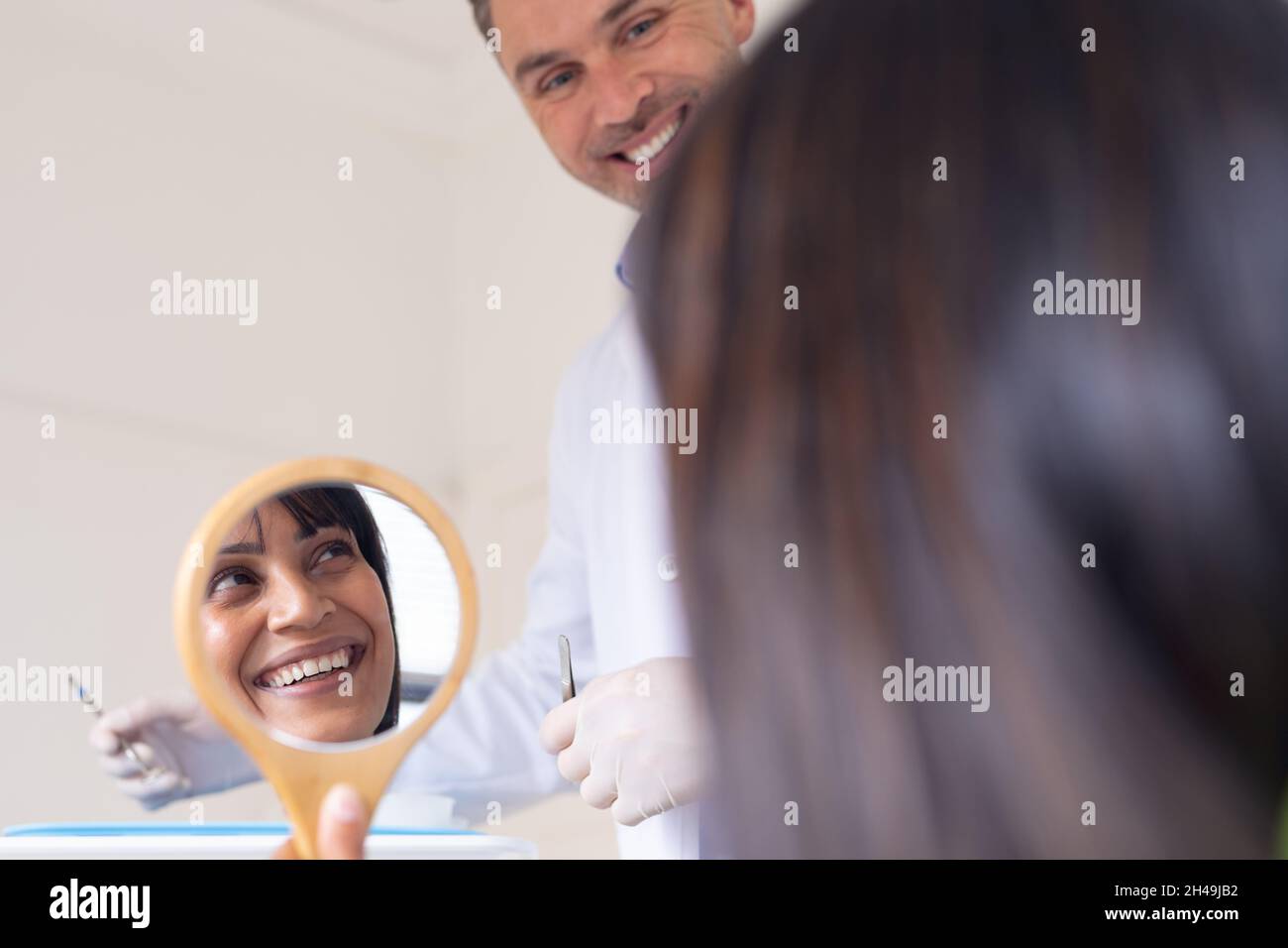 Smiling caucasian male dentist with female patient looking at mirror at ...