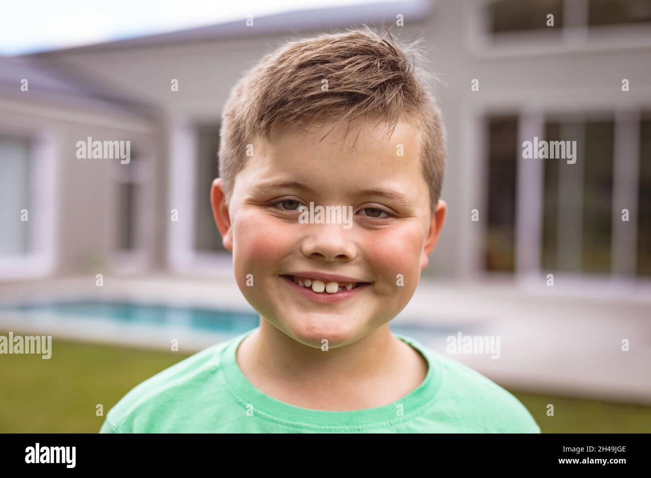 Portrait of smiling caucasian boy with brown hair standing at backyard ...