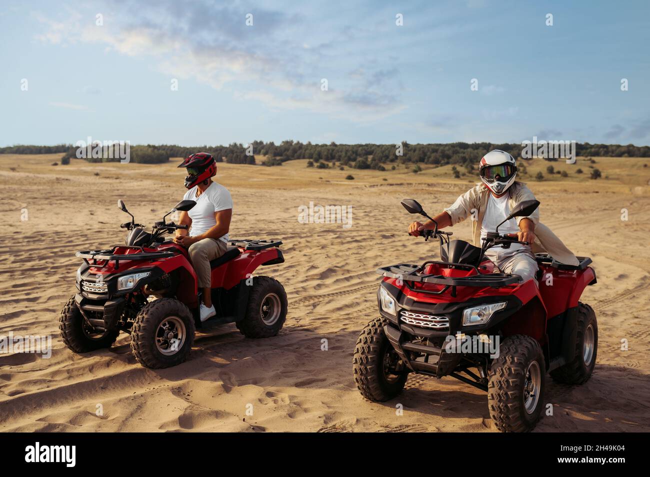 Two men in helmets ride on atv in desert Stock Photo - Alamy