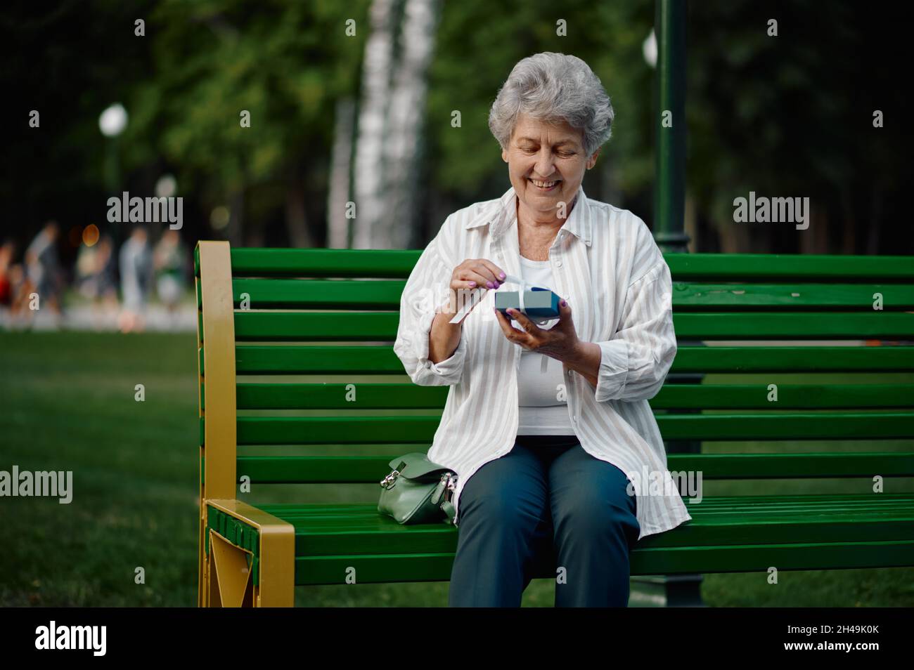 Cheerful granny opens a gift box on the bench Stock Photo - Alamy