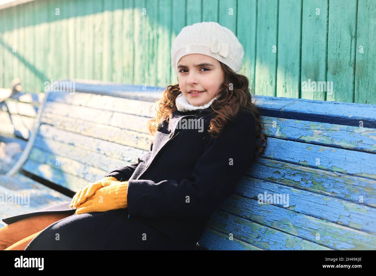 little girl in a blue coat on a park bench in autumn. High quality ...