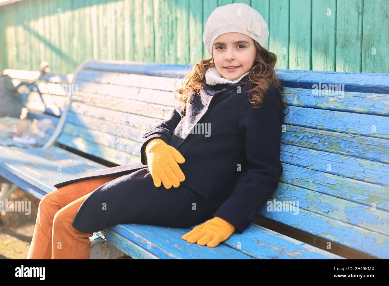 little girl in a blue coat on a park bench in autumn. High quality ...
