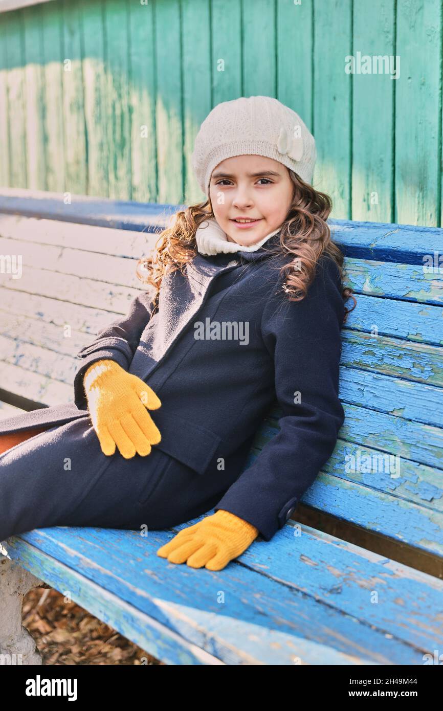 little girl in a blue coat on a park bench in autumn. High quality ...