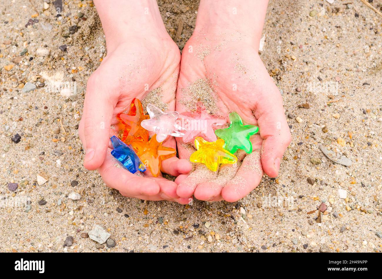 Multicolored decorative stars in hands on the background of beach sand ...