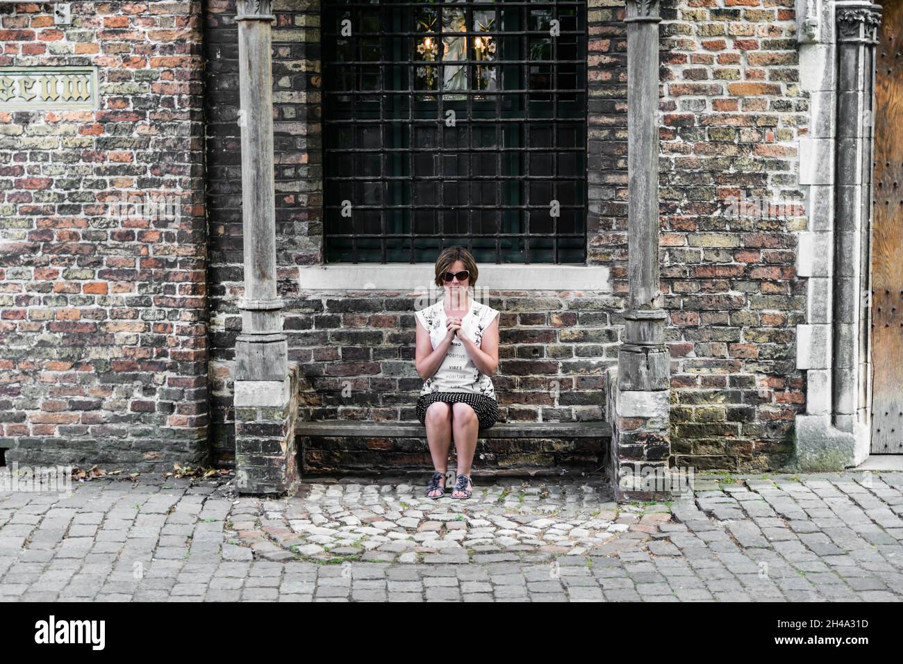 Playful tourist sitting as a prayer on an old bench, Bruges, Belgium ...
