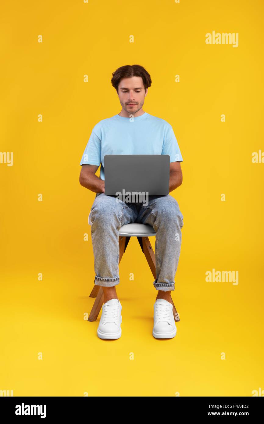 Portrait of serious bearded guy sitting on chair using laptop computer ...