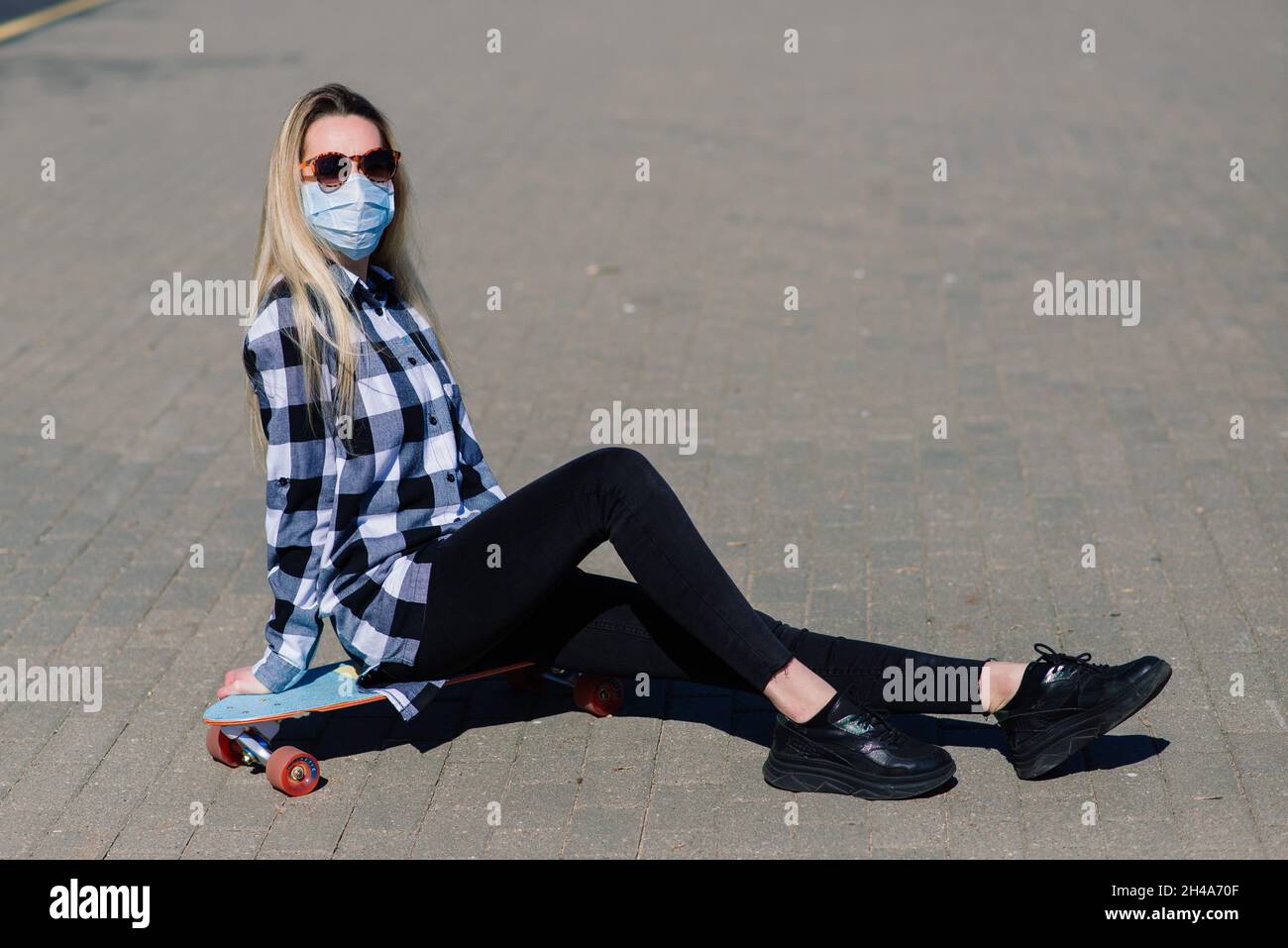Portrait of a young female in a medical mask with longboard in the city ...