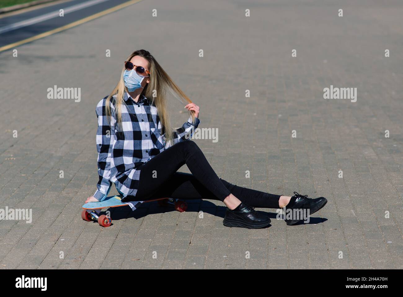 Portrait of a young female in a medical mask with longboard in the city during the quarantine ...