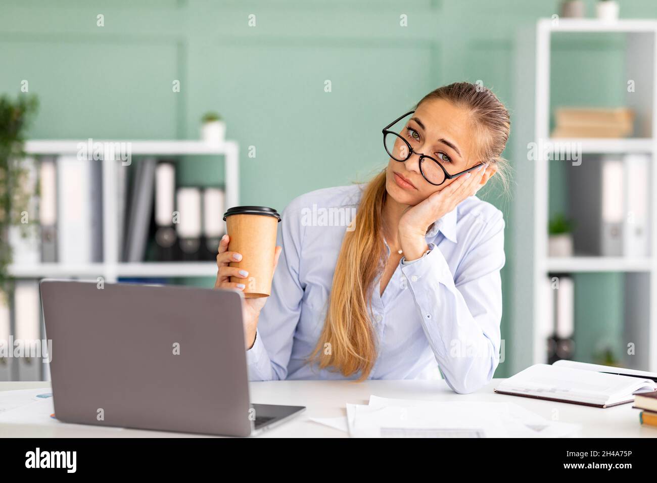 Portrait of tired young office worker sitting at workplace with laptop ...