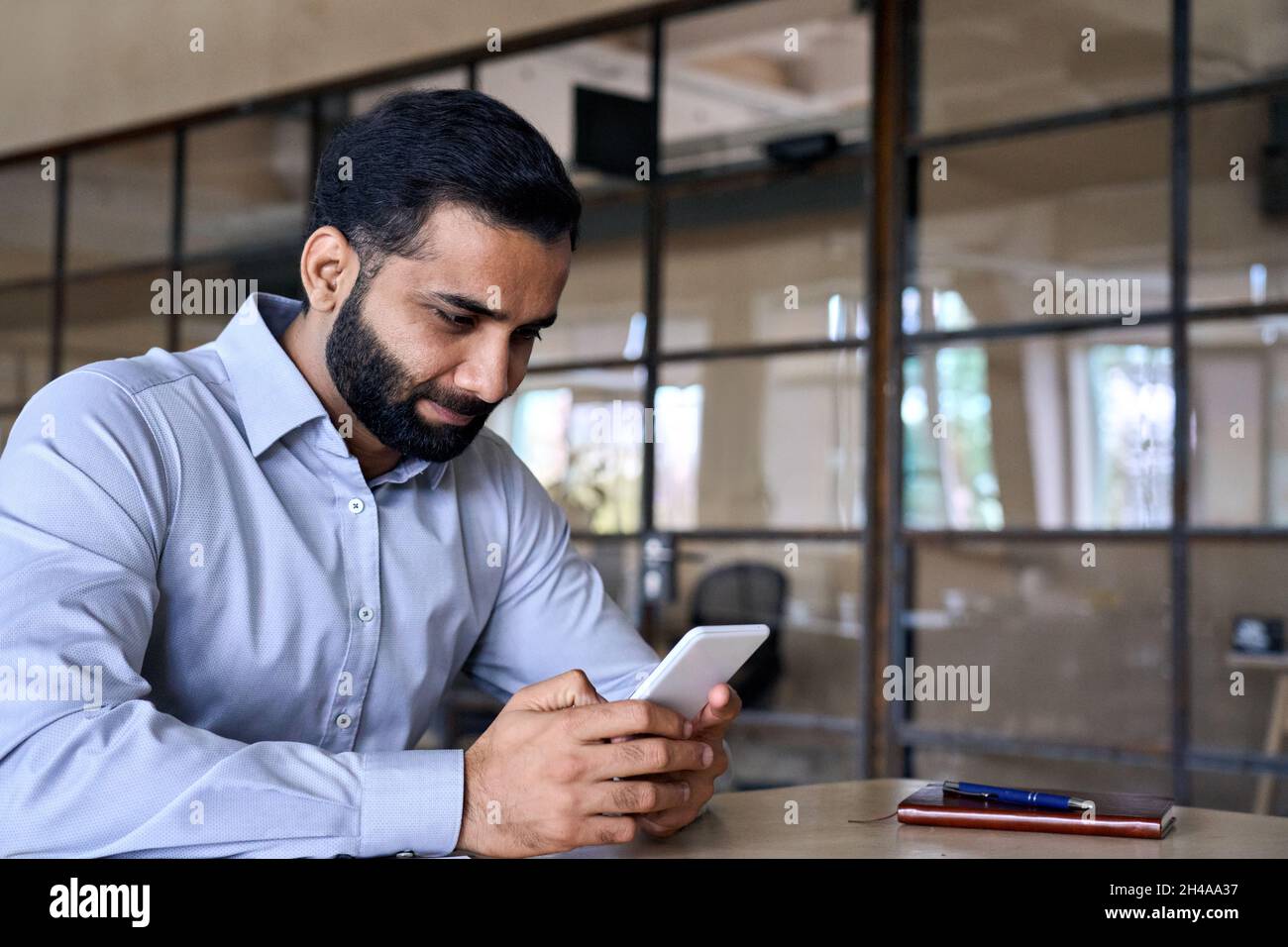 Smiling indian ceo businessman holding phone in modern office desk ...