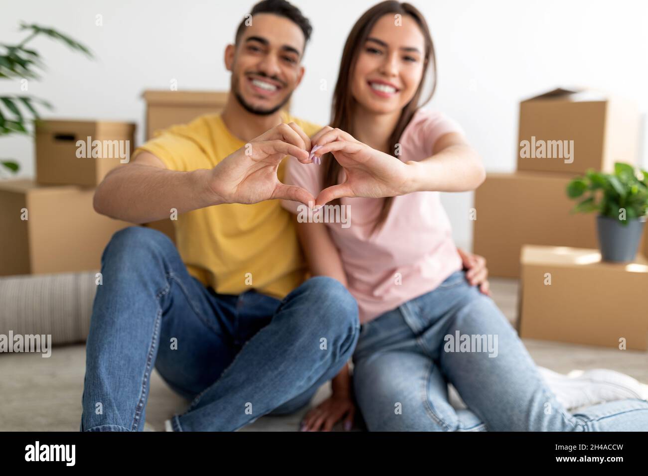 Affectionate young multiracial couple making heart gesture with their hands, moving to new house ...