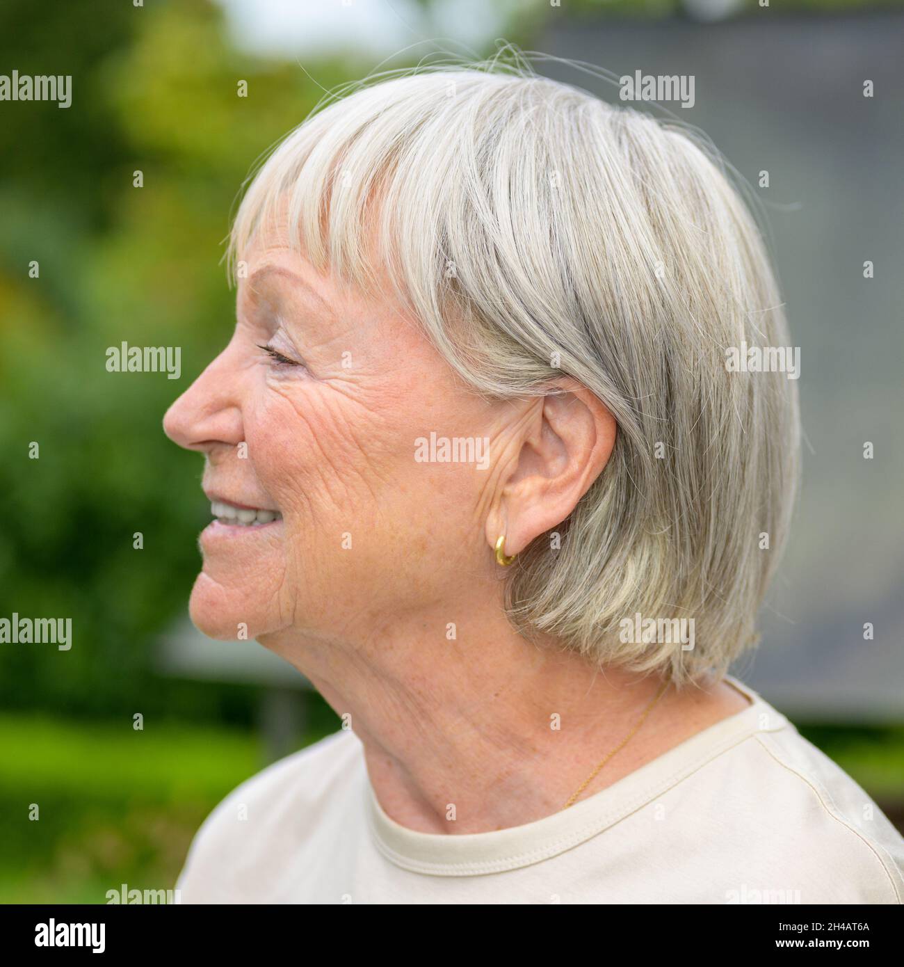 Profile portrait of a smiling happy senior lady outside in a garden ...