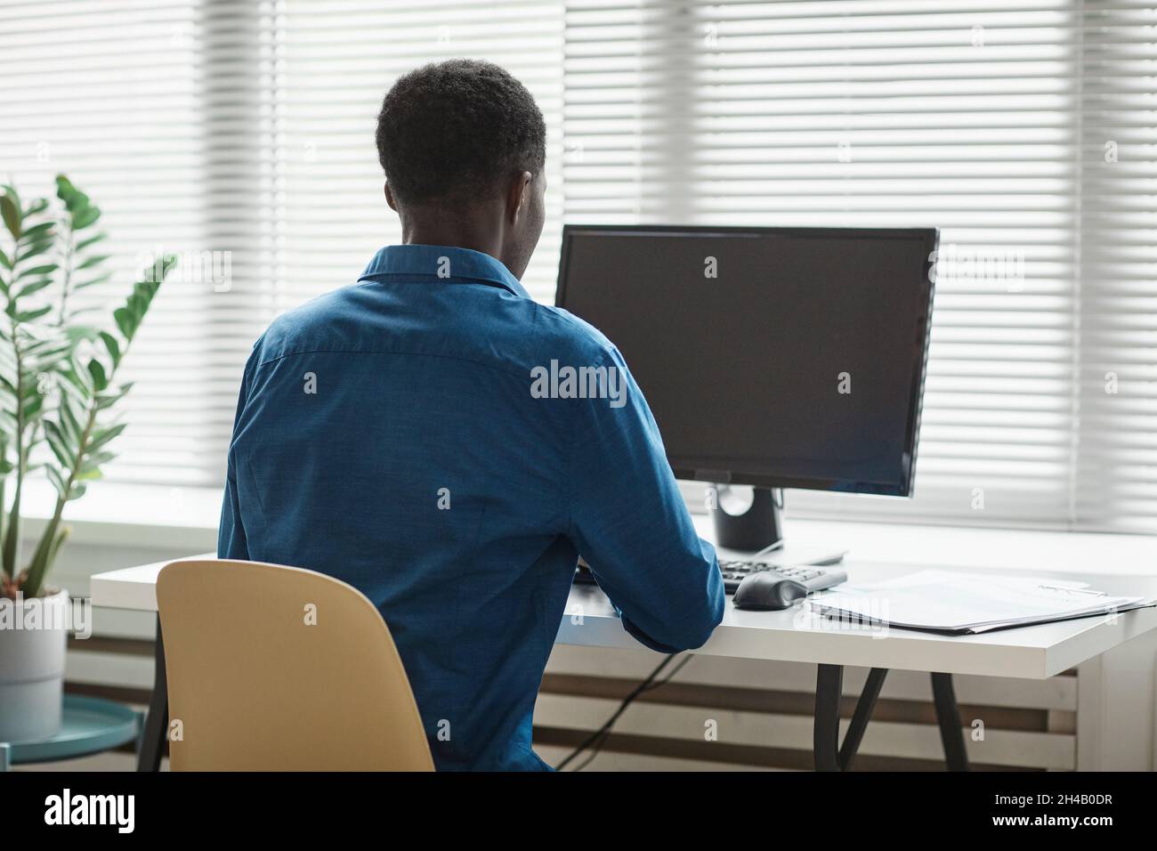 Back view at African-American man using computer at desk by window ...