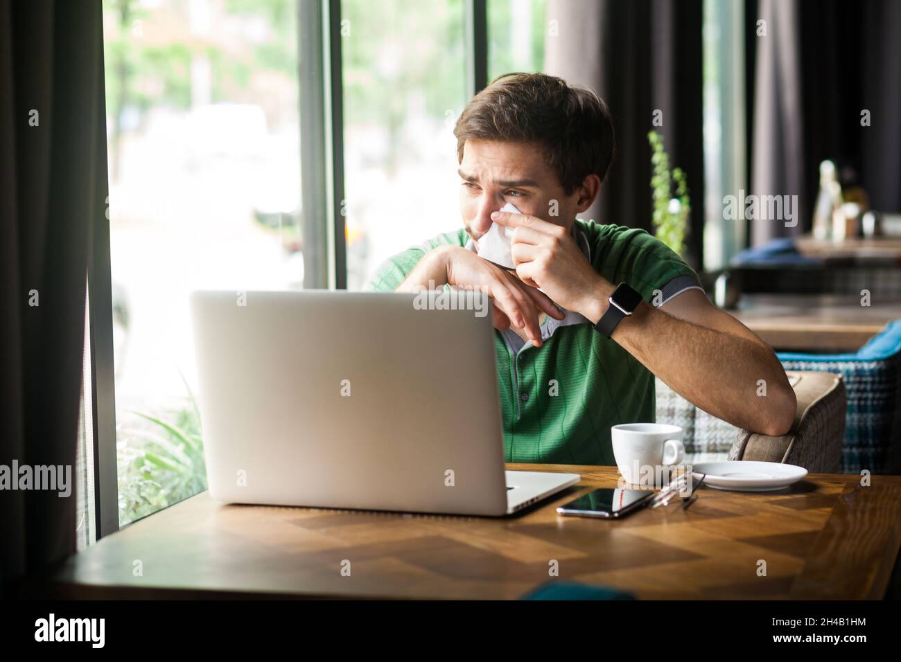 Portrait of upset businessman wearing green T-shirt, sitting in front ...
