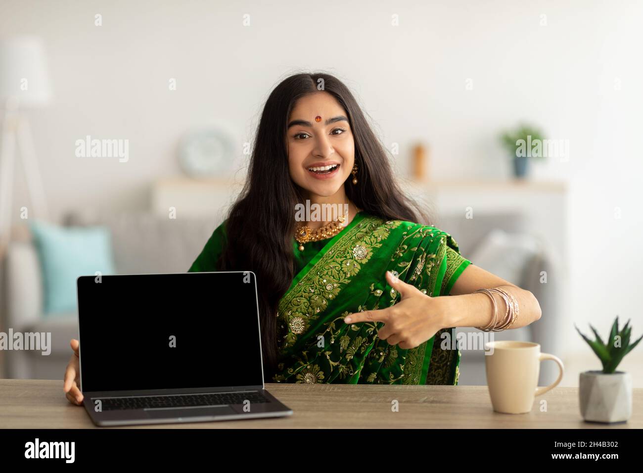Cheerful Indian woman in green sari dress pointing at laptop computer ...