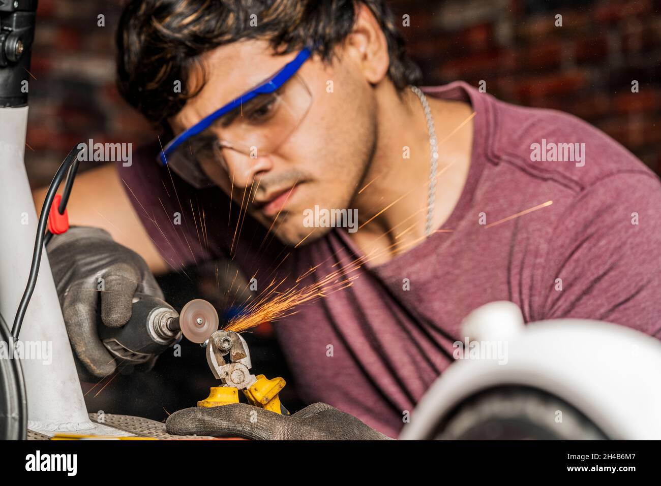 A focused mechanic wearing safety goggles using a mini grinder to cut a ...
