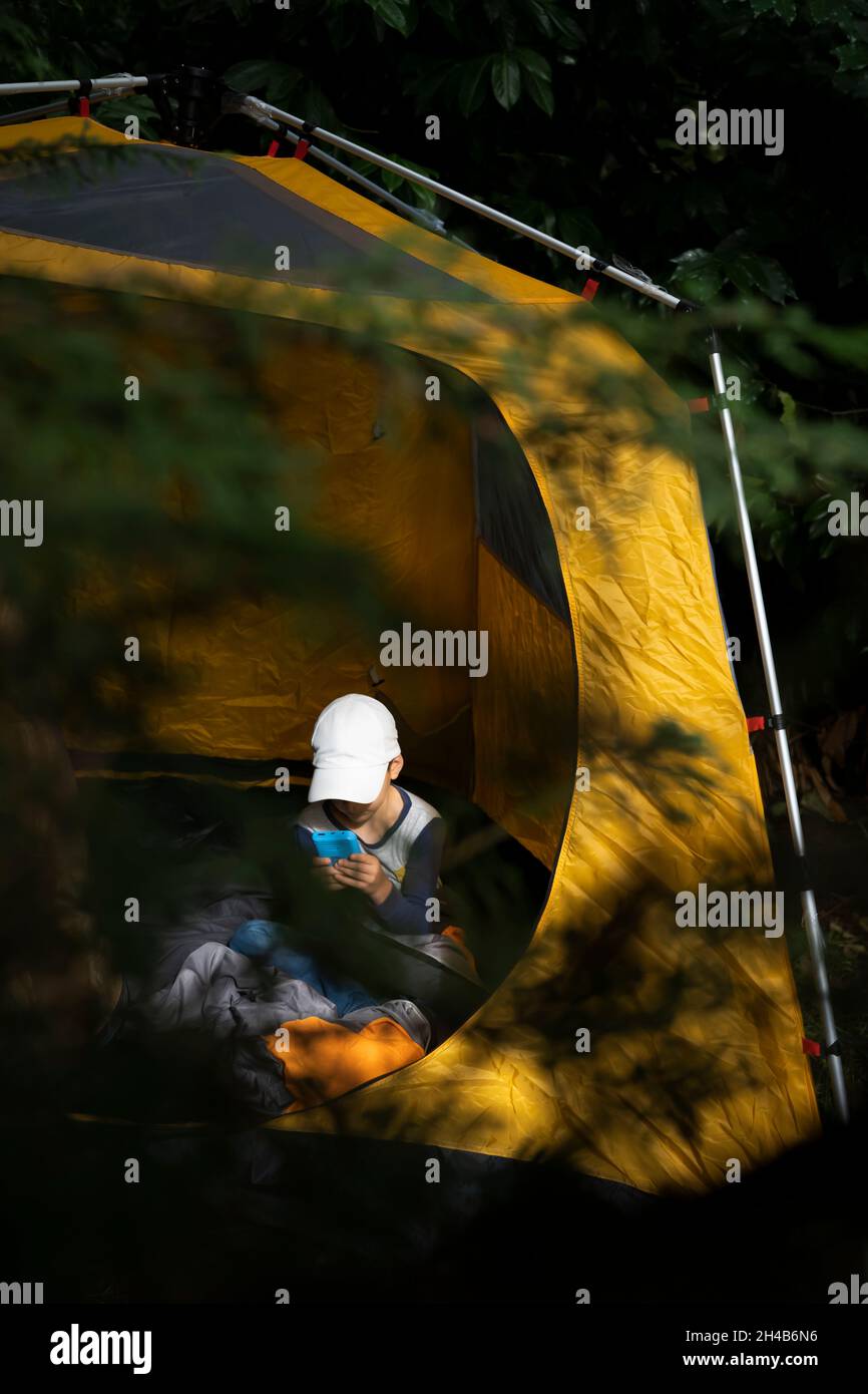Boy playing on retro game console in tent at campsite during vacation ...