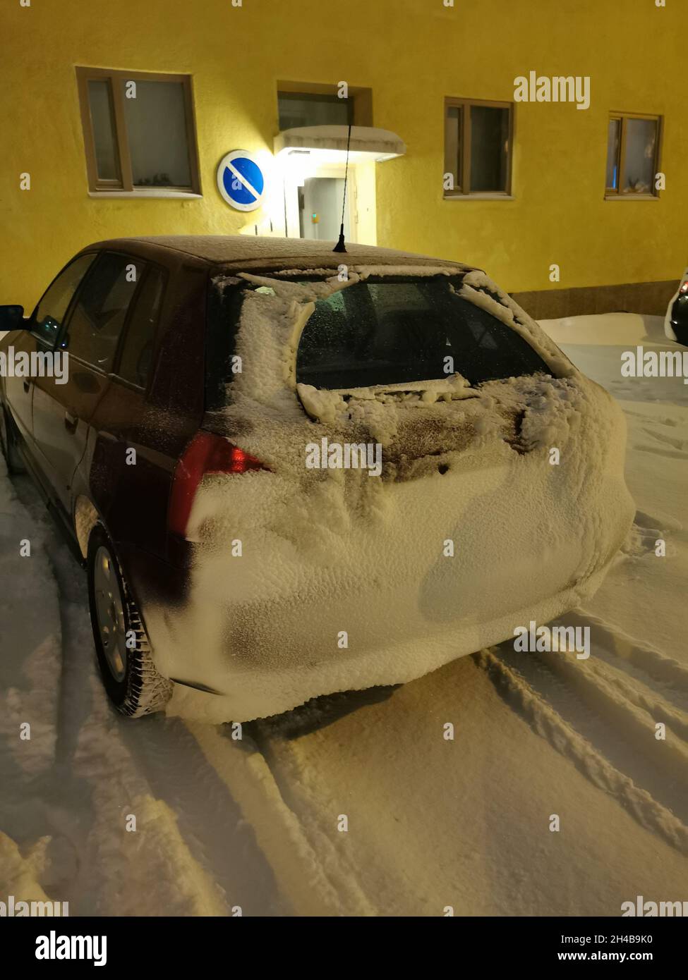 Back of a red car frozen with lot of snow in front of a yellow house ...