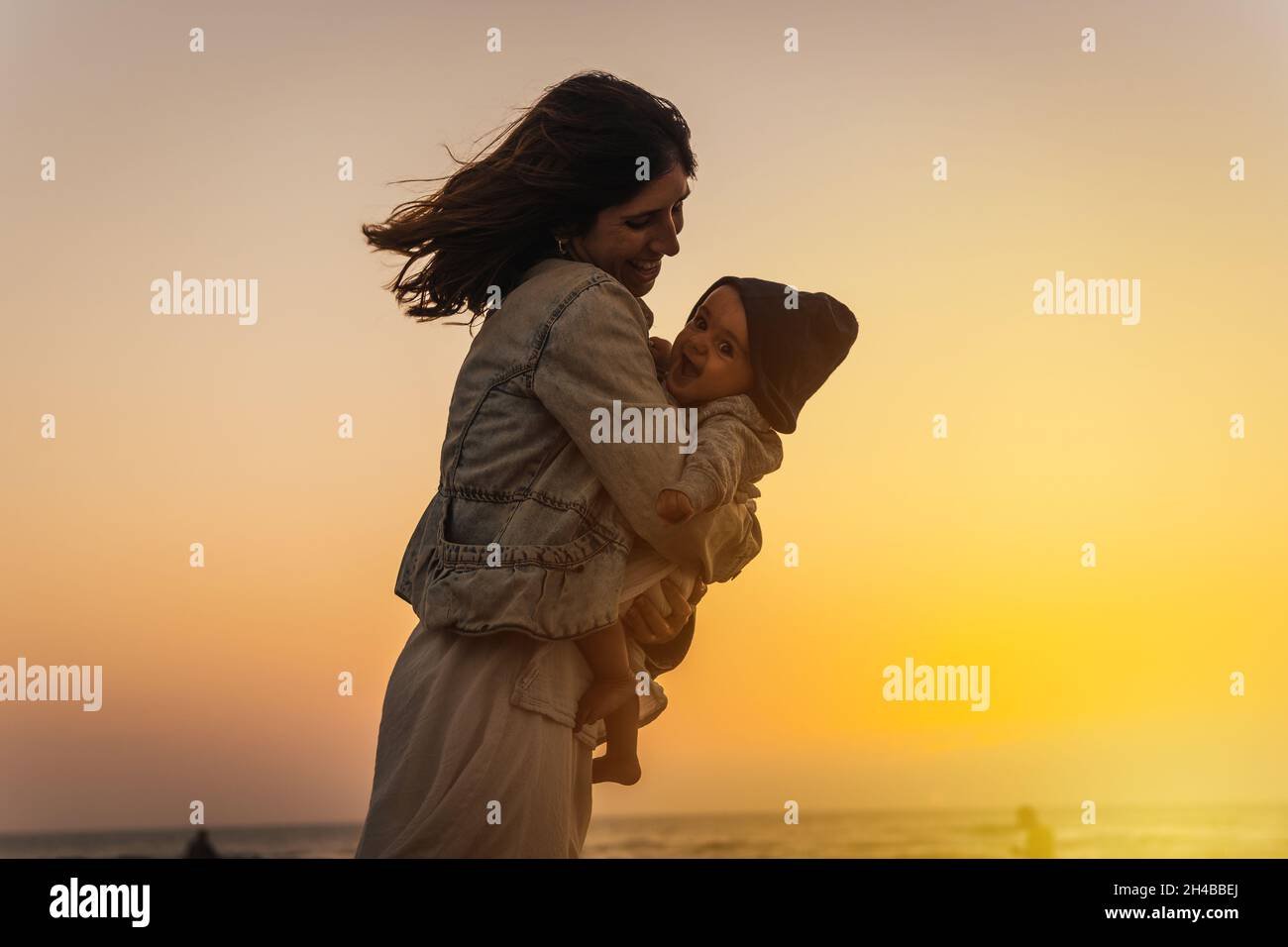 Young mother hugging her son with a sunset background in Punta Ballena ...