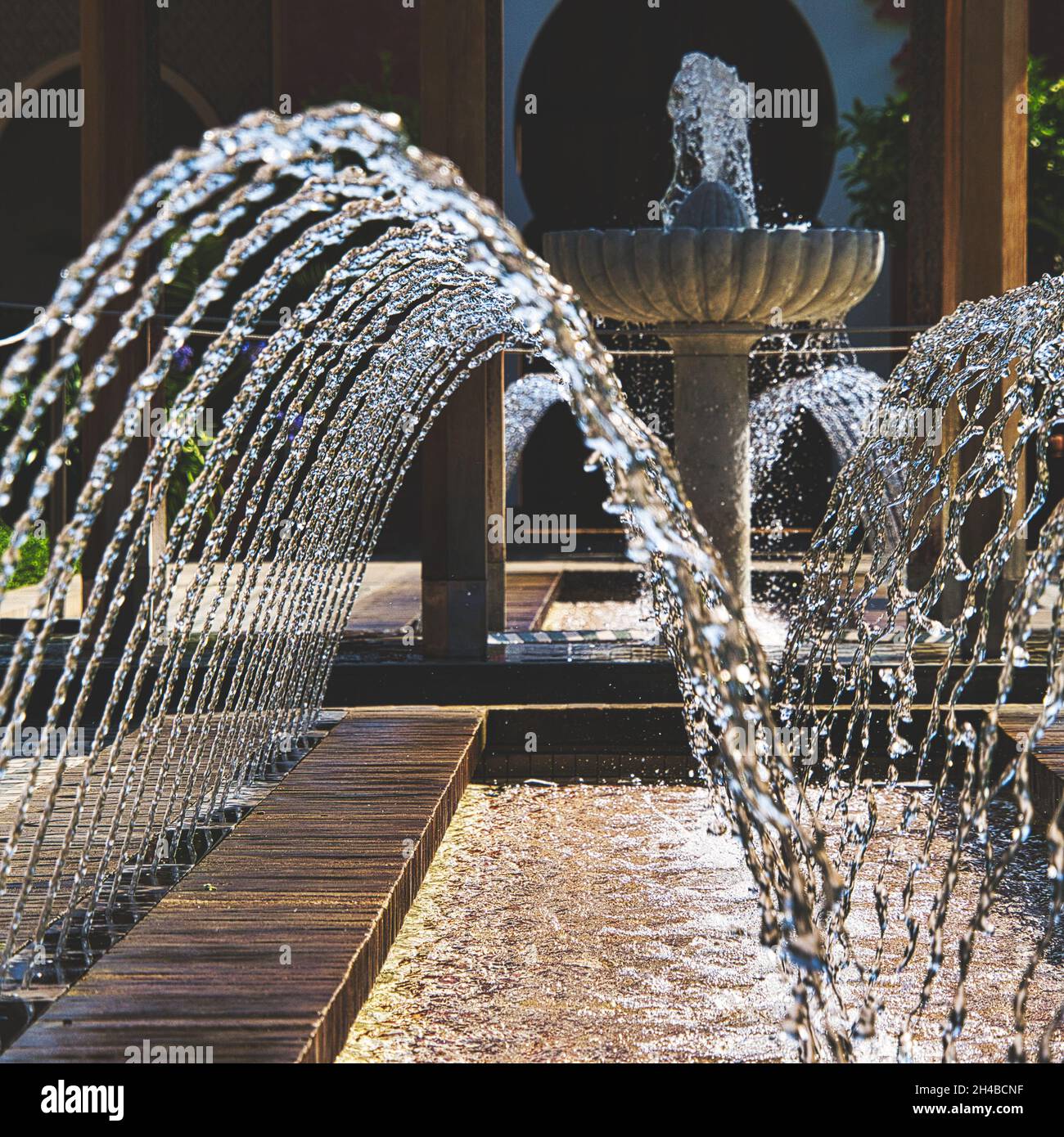 Modern designed jet fountains splashing water in a wooden shallow pool ...