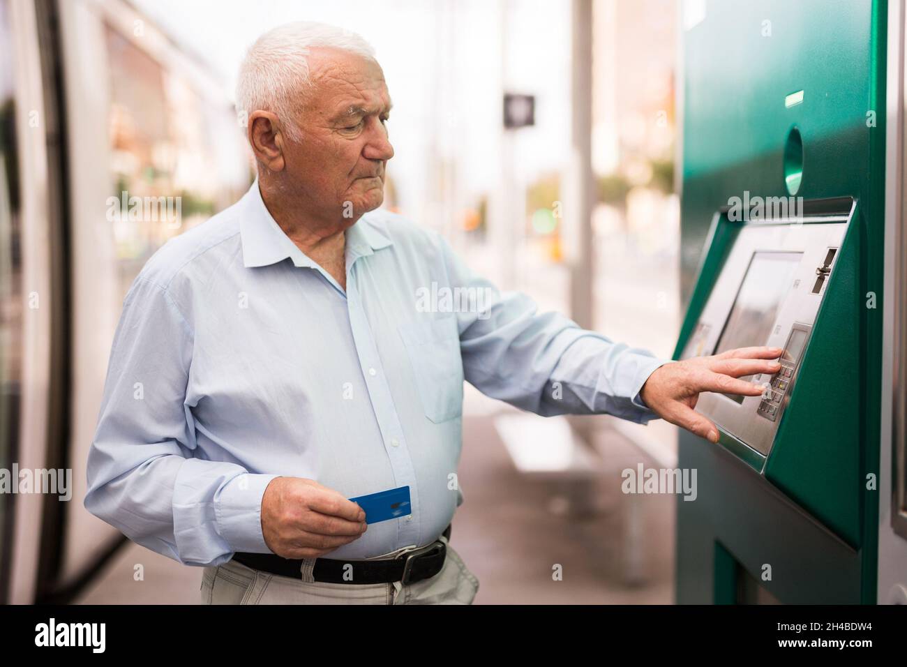 Old man using cash machine on tram station Stock Photo - Alamy