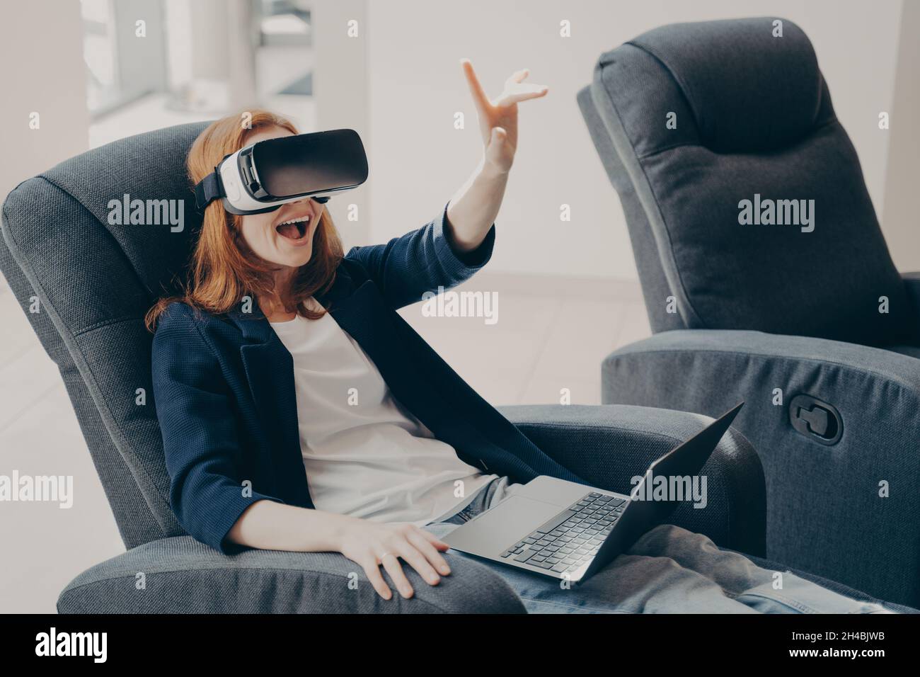 Surprised excited woman in VR headset goggles and laptop, sitting in ...