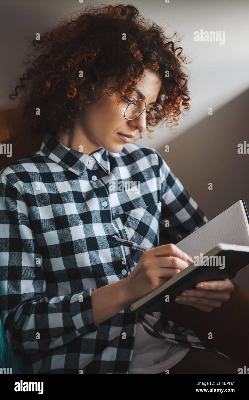 Curly woman notes something in her notebook. Planning the day. Home ...