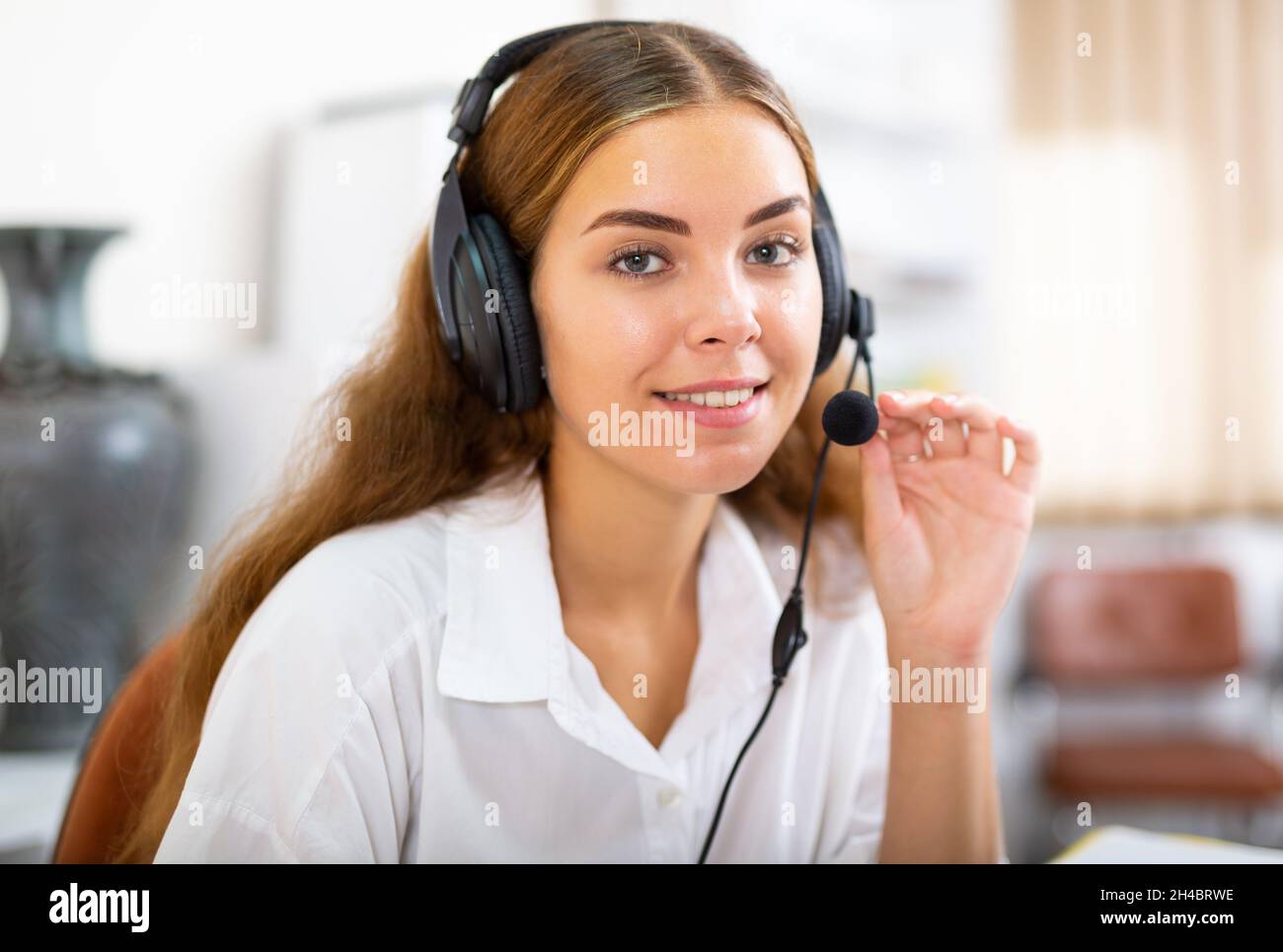 Portrait of a smiling young operator girl in the office with headphones ...