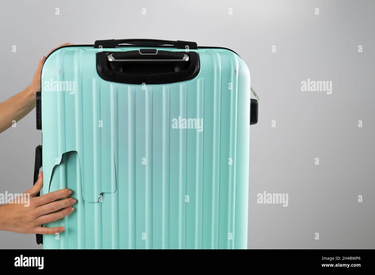 A woman demonstrates a broken suitcase on a white background. Damaged ...