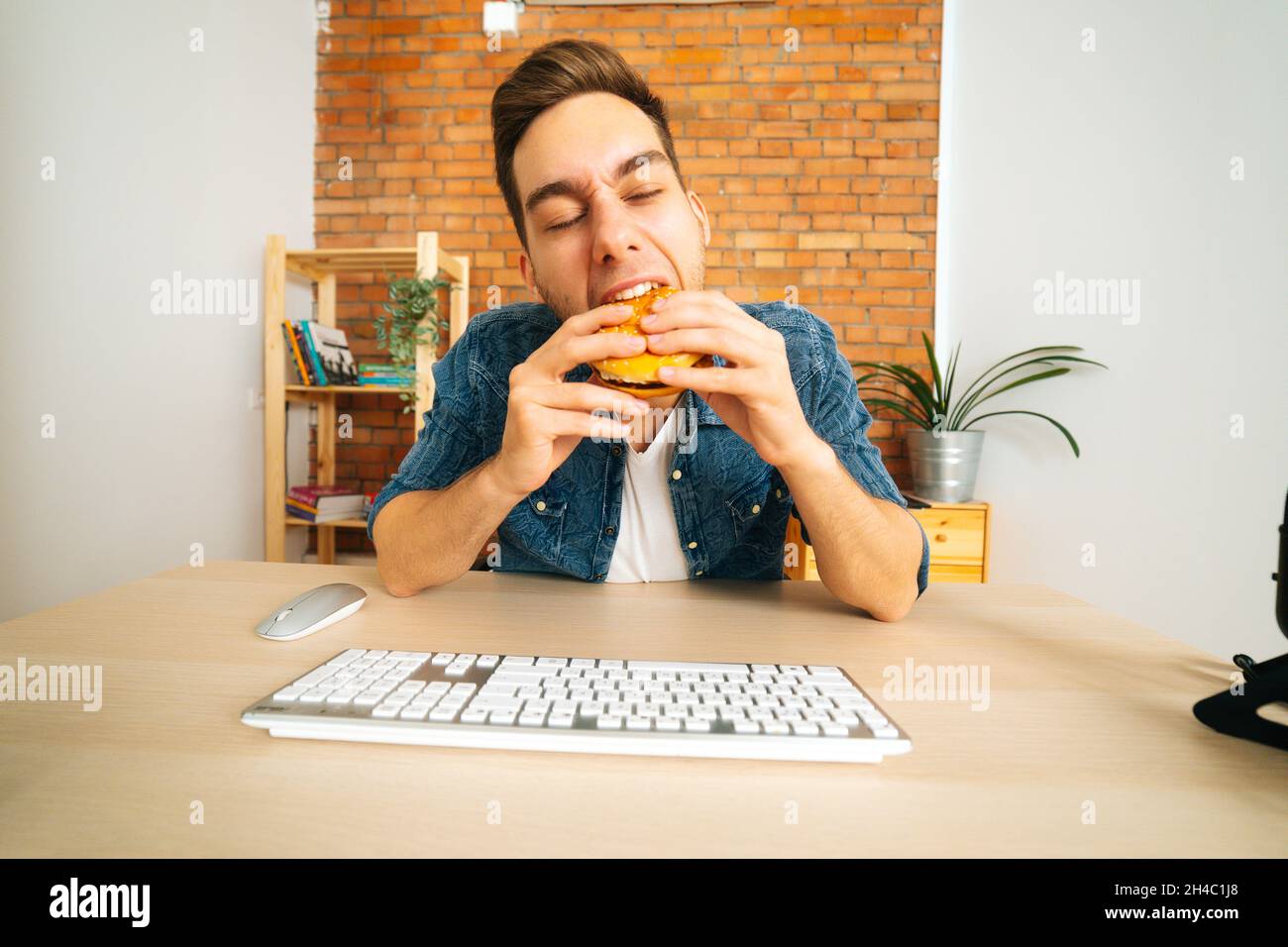 Front view of handsome hungry young man eating hamburger with beef from ...