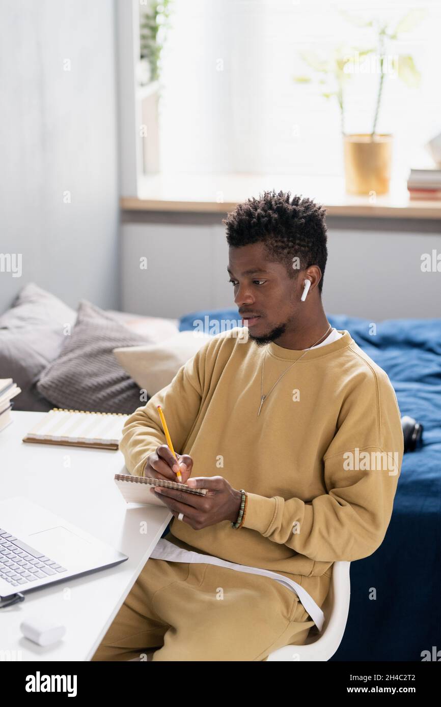Serious young African student making notes in notepad while sitting by ...