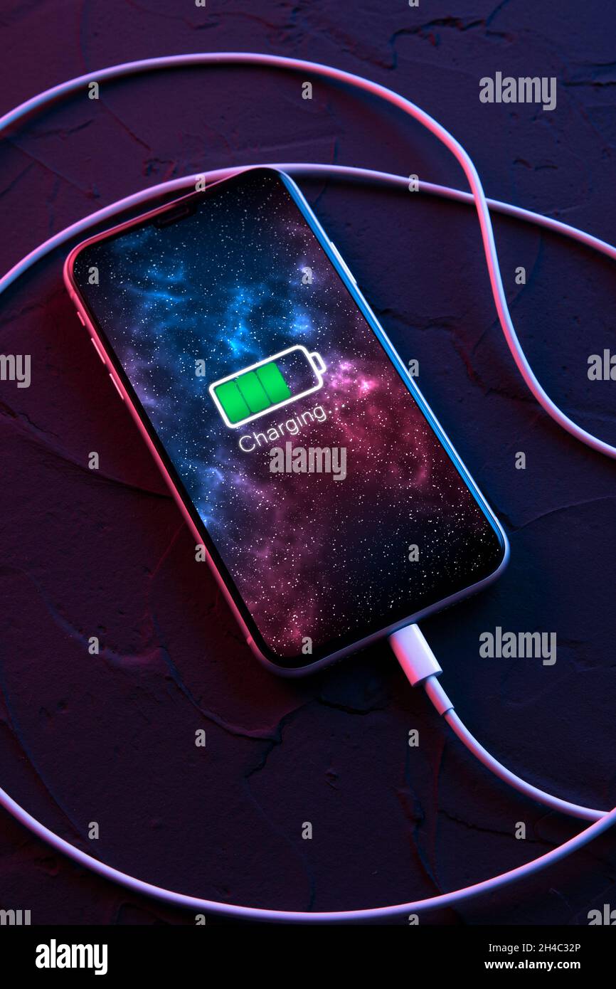 Mobile smart phone on wireless charging device on dark neon red and ...