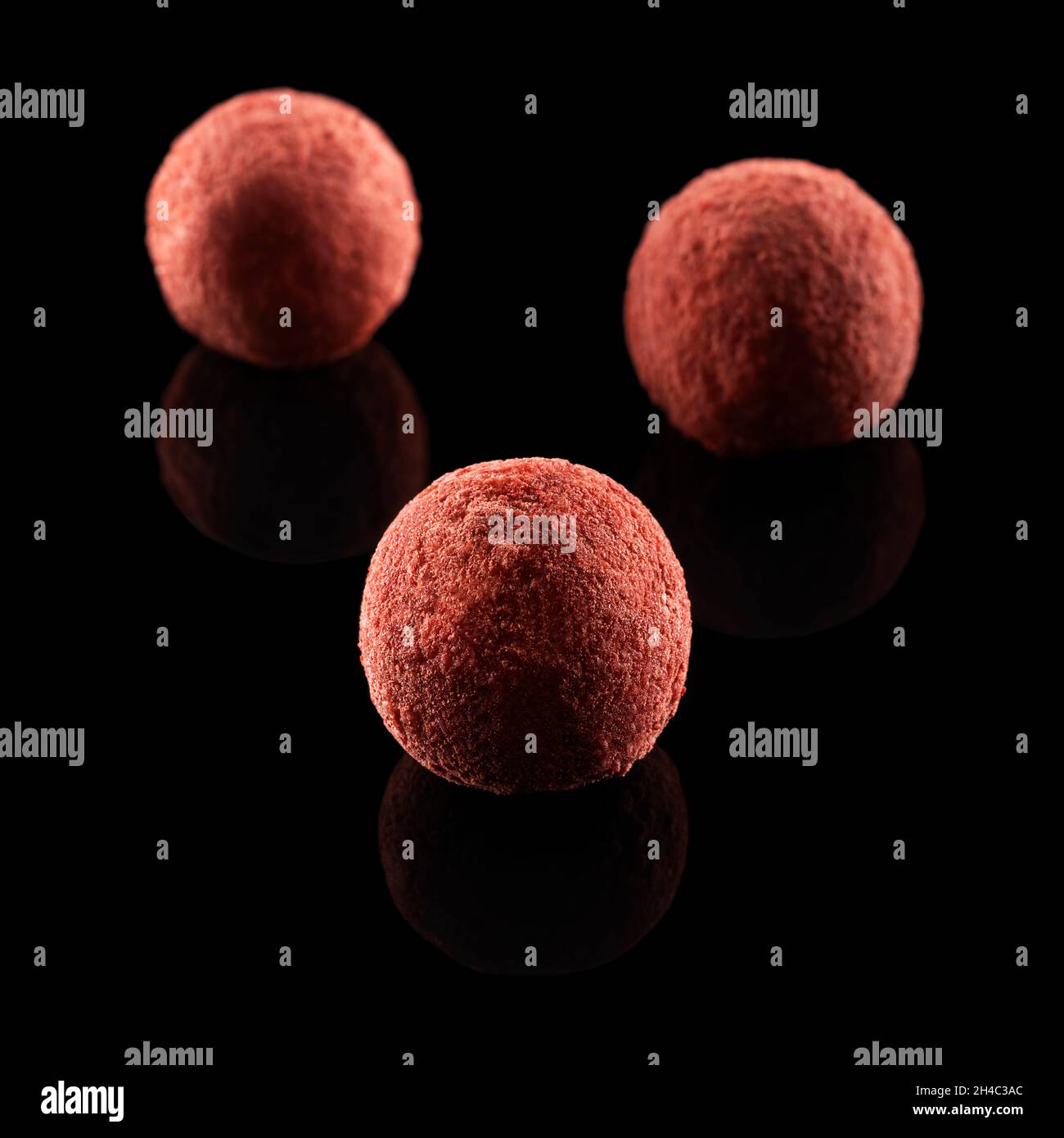 Three strawberry truffles isolated on a black background. Front view ...