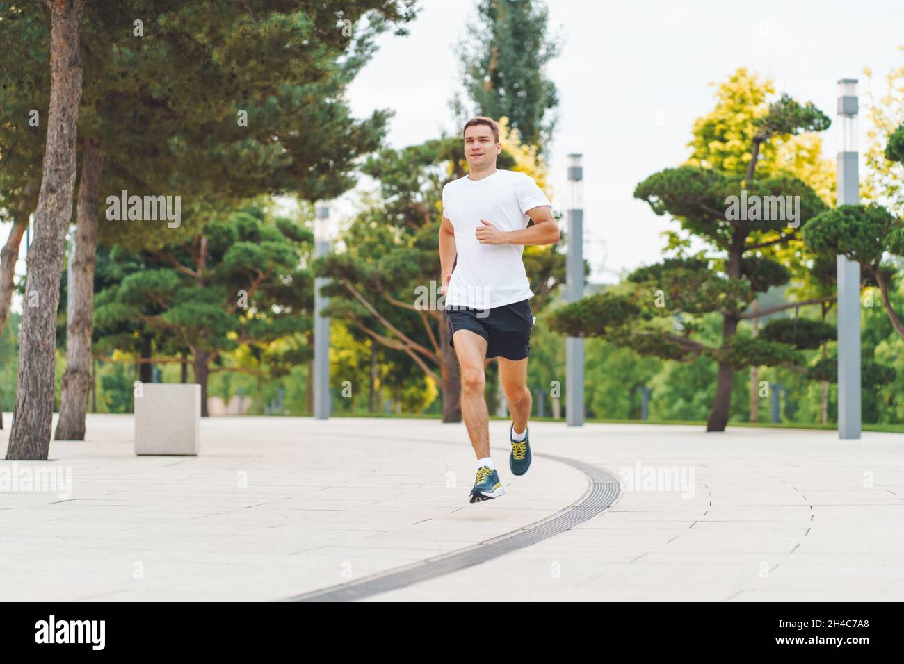 Attractive young man athlete wearing sportswear run in modern park at ...
