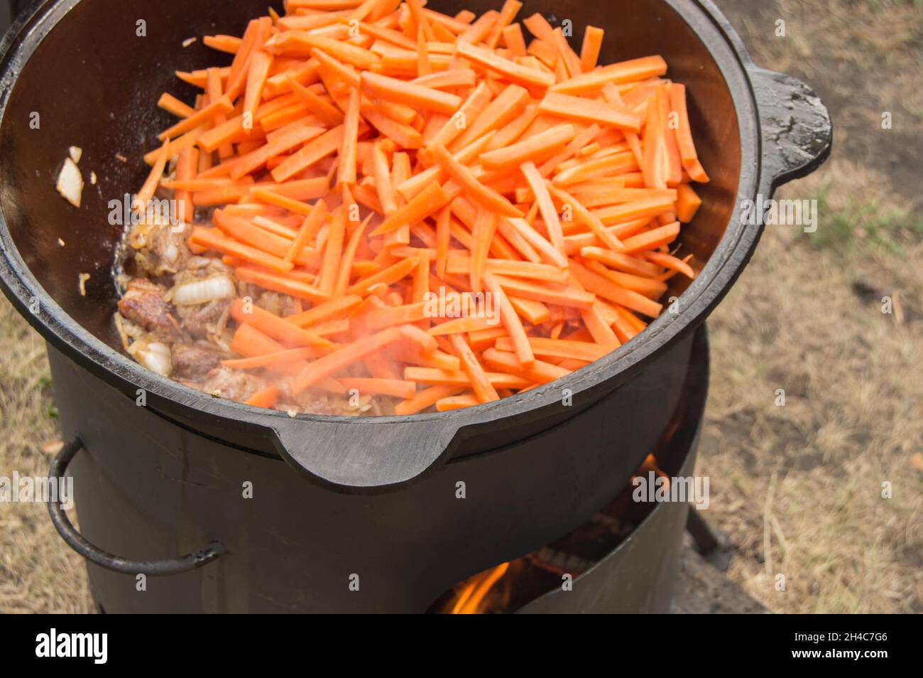 Cooking pilaf in a cast-iron wok in the open air. Lots of sliced ...