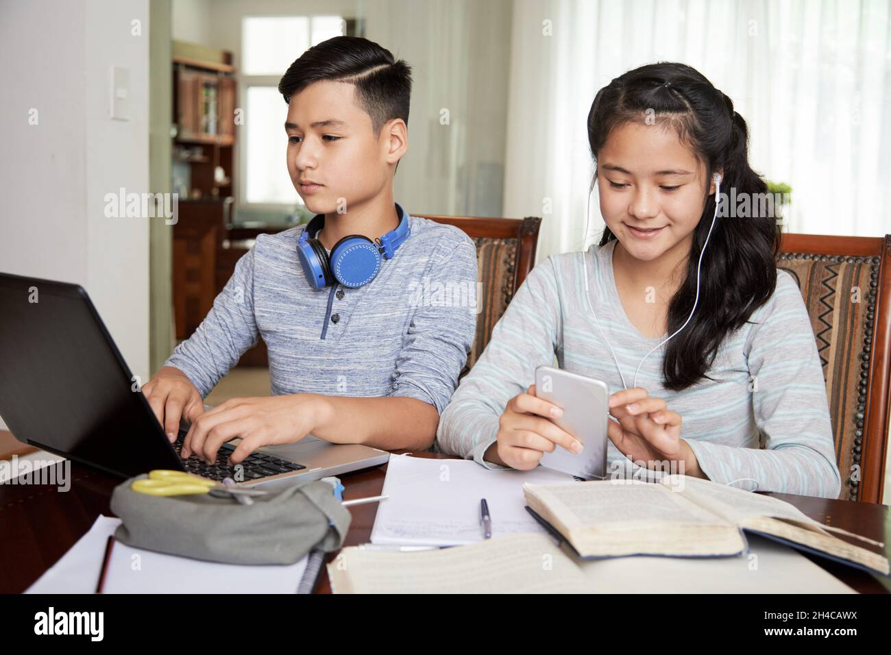 Smiling teenage brother and sister doing homework together at home for ...