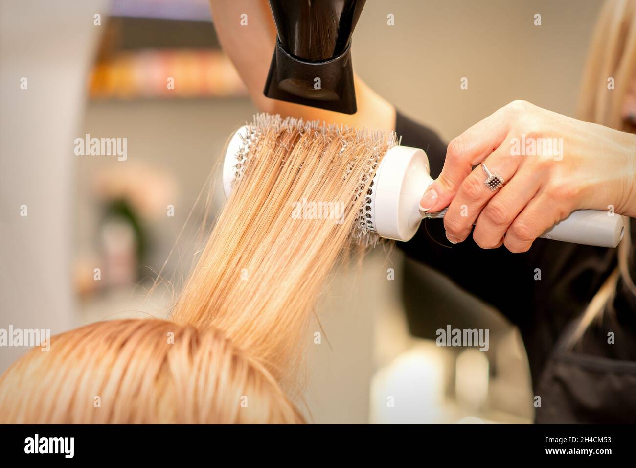Professional hairdresser dry hair with a hairdryer and round hairbrush ...