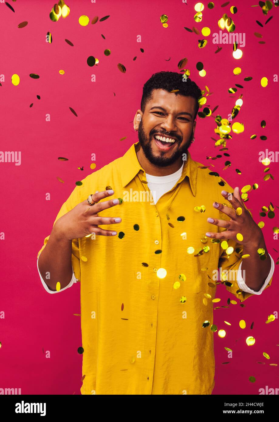 Golden confetti in the studio. Excited young man smiling cheerfully ...