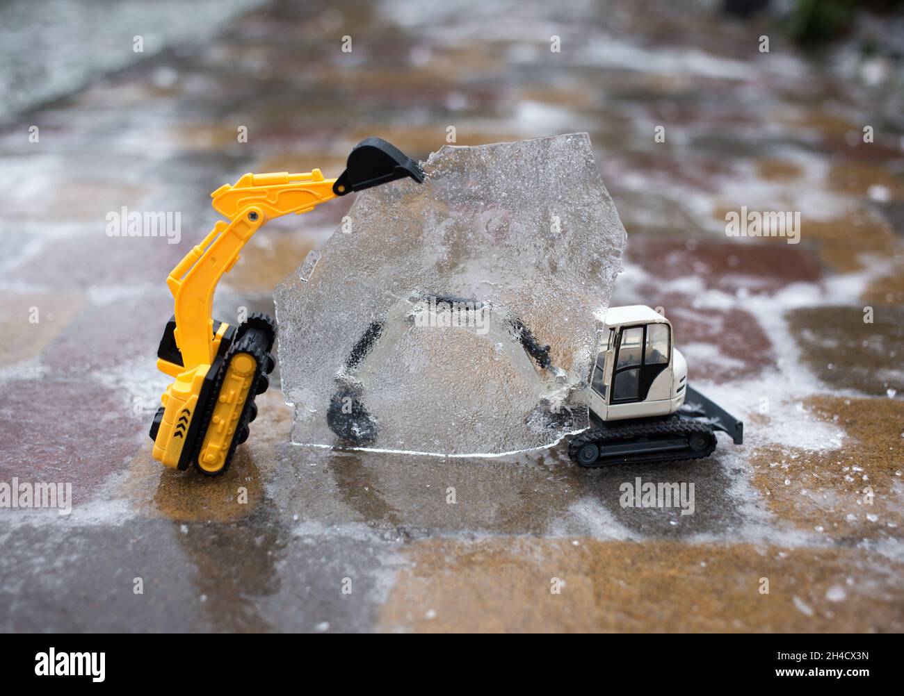 2 toy excavators standing on an icy road. The excavator boom is holding ...