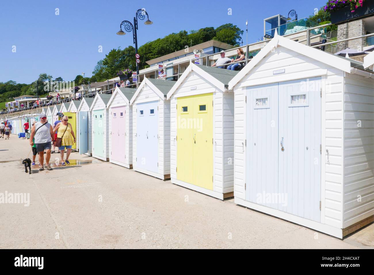 People walking past the pastel coloured Beach huts Lyme Regis beach ...