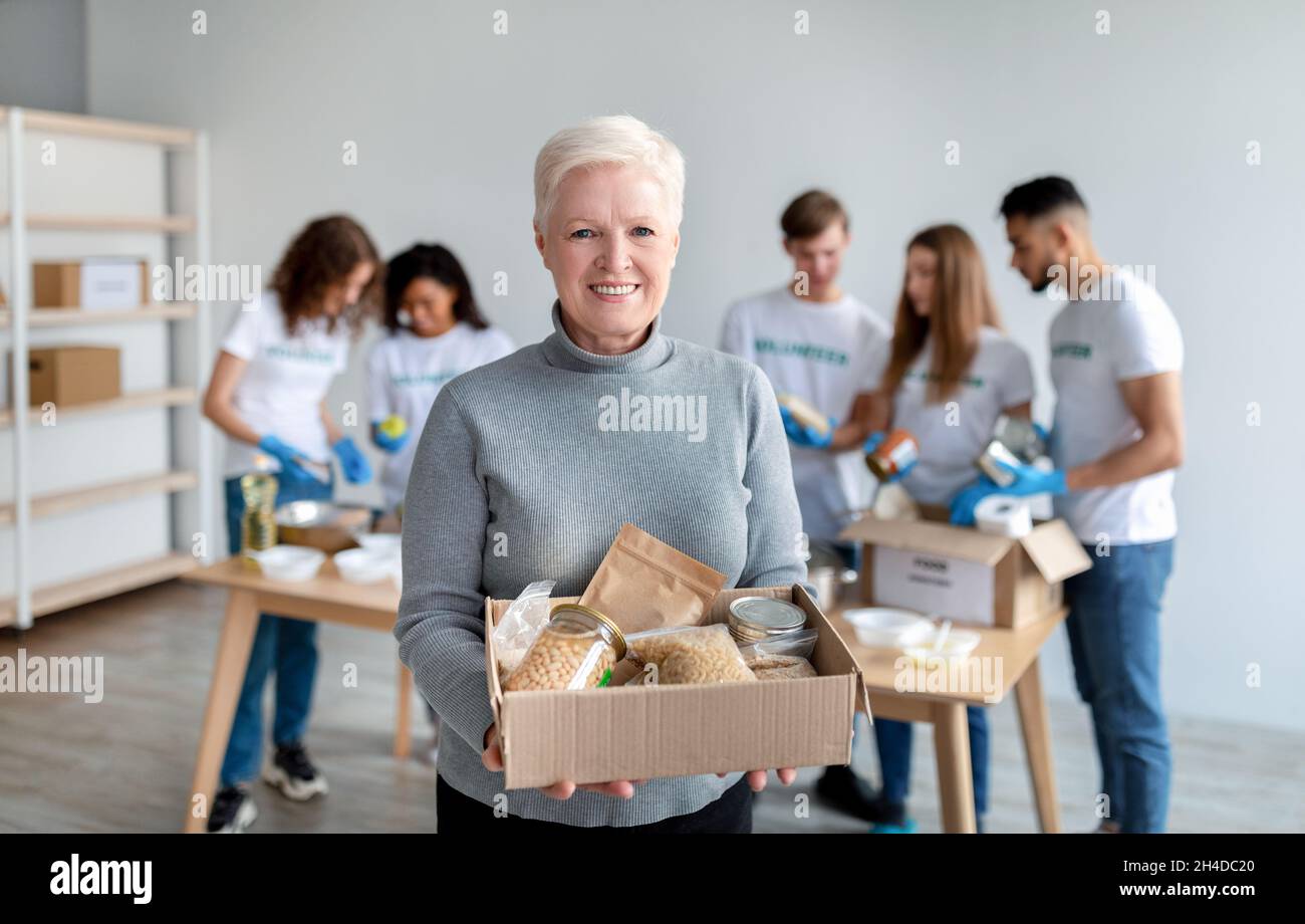 Happy senior woman holding box with donations food and smiling at ...