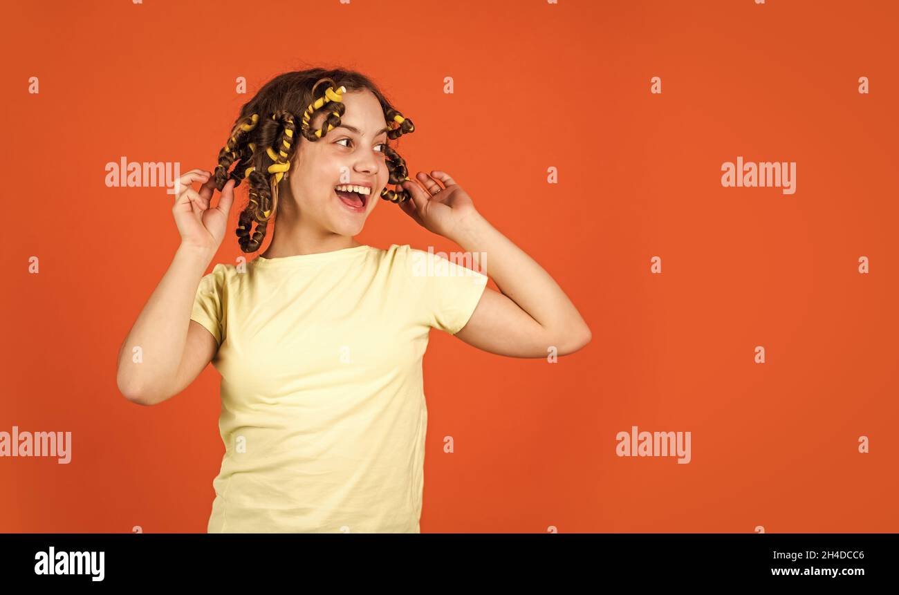 Styling tips. Small girl Curling Hair Using Curlers orange background ...