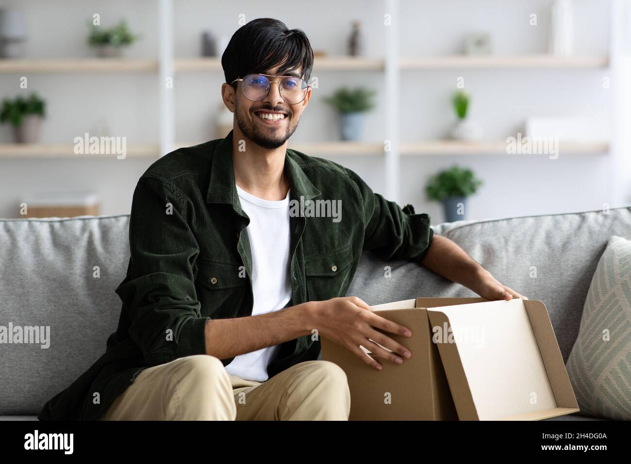 Smiling arabic guy opening paper box, home interior Stock Photo - Alamy