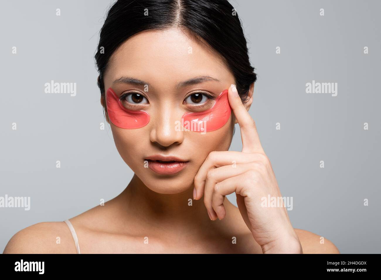 Pretty asian woman in eye patches looking at camera isolated on grey ...