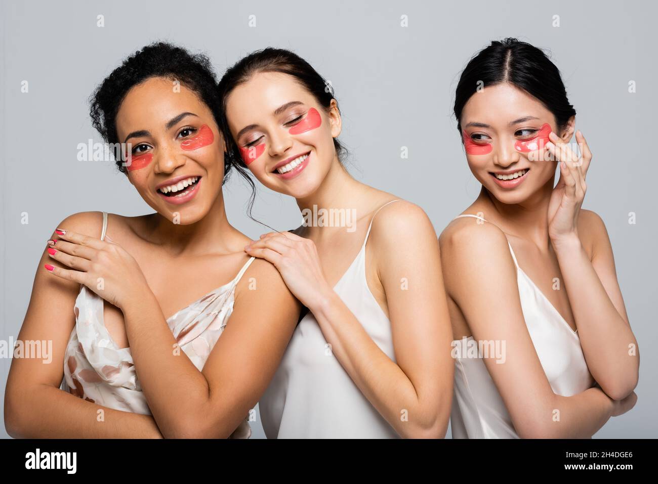 Cheerful multicultural friends in eye patches and satin dresses posing ...