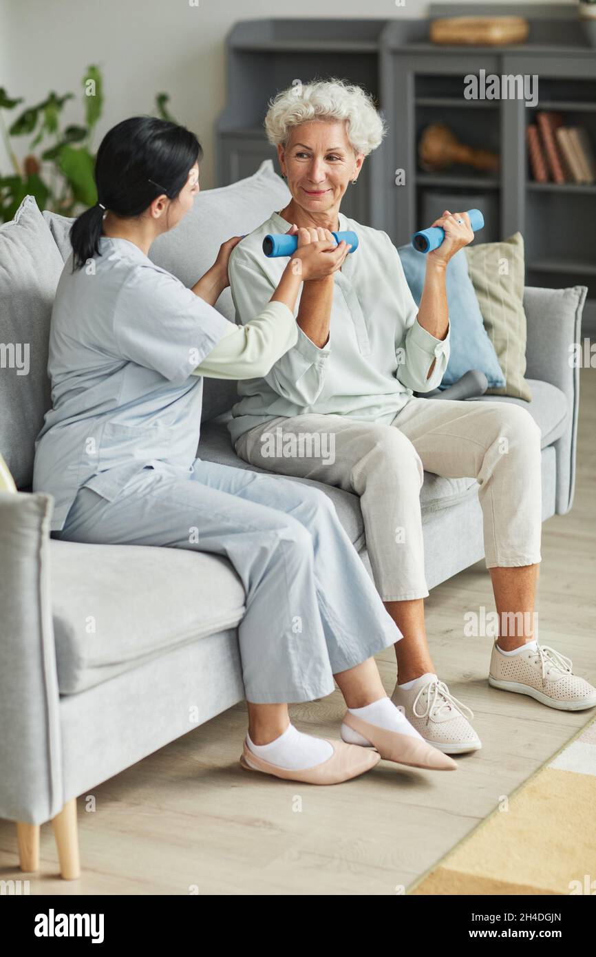 Vertical full length portrait of female nurse helping senior woman in ...
